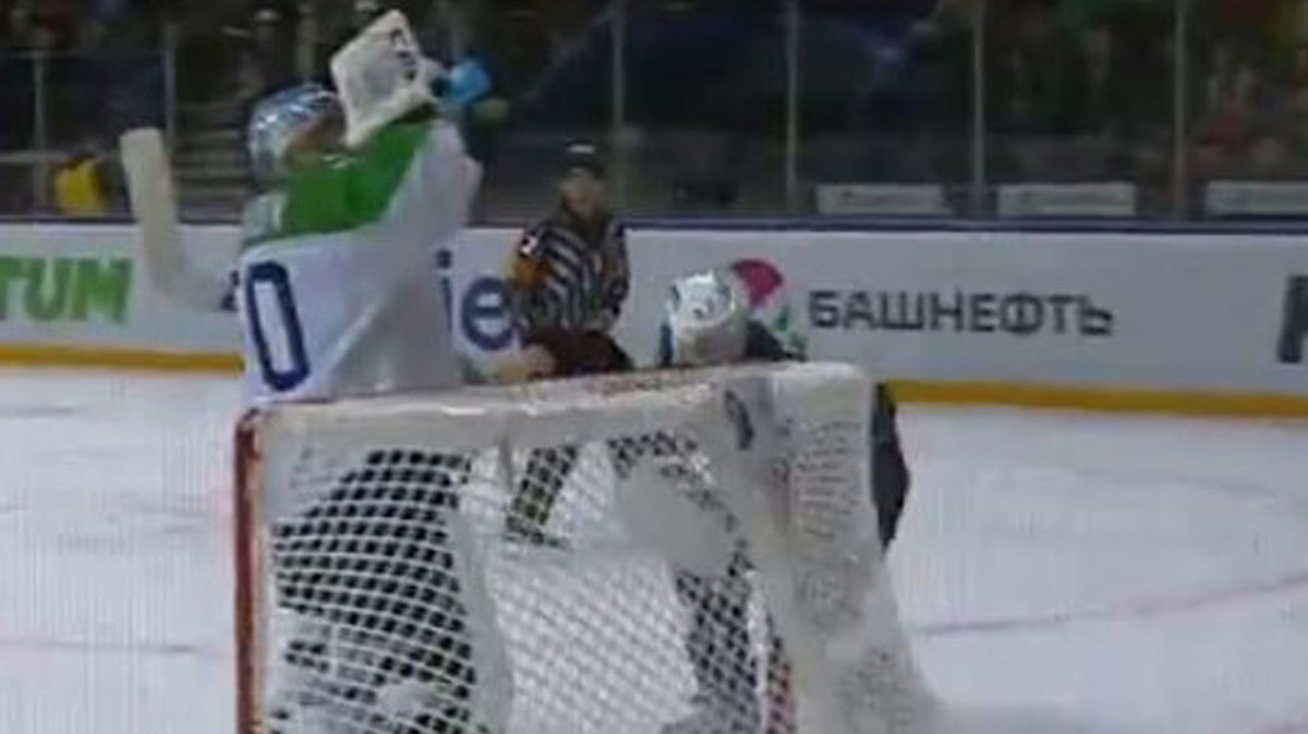 Ice hockey goalie takes a drink as play goes on around him